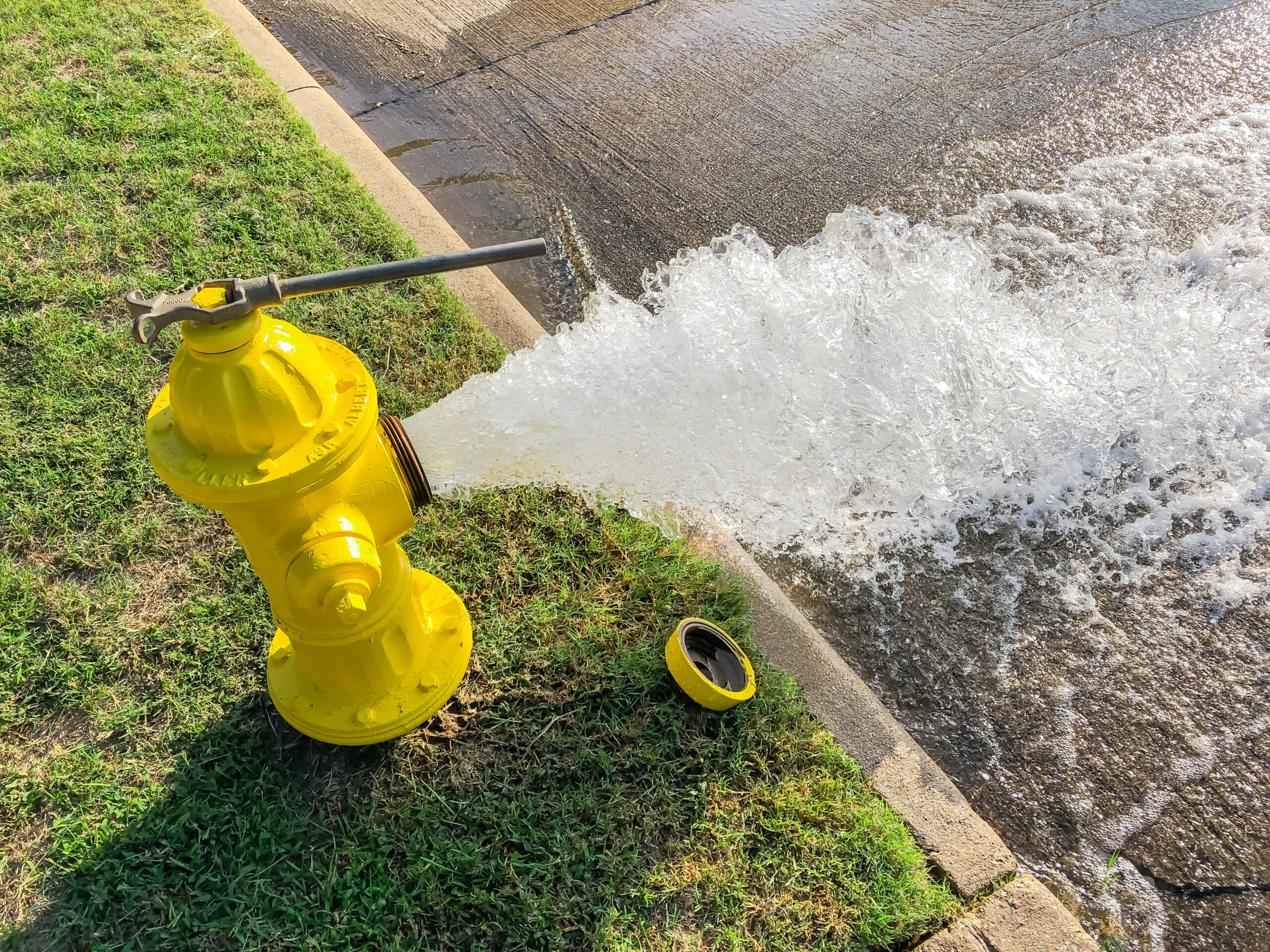 Top view yellow fire hydrant gushing water across a residential street ...